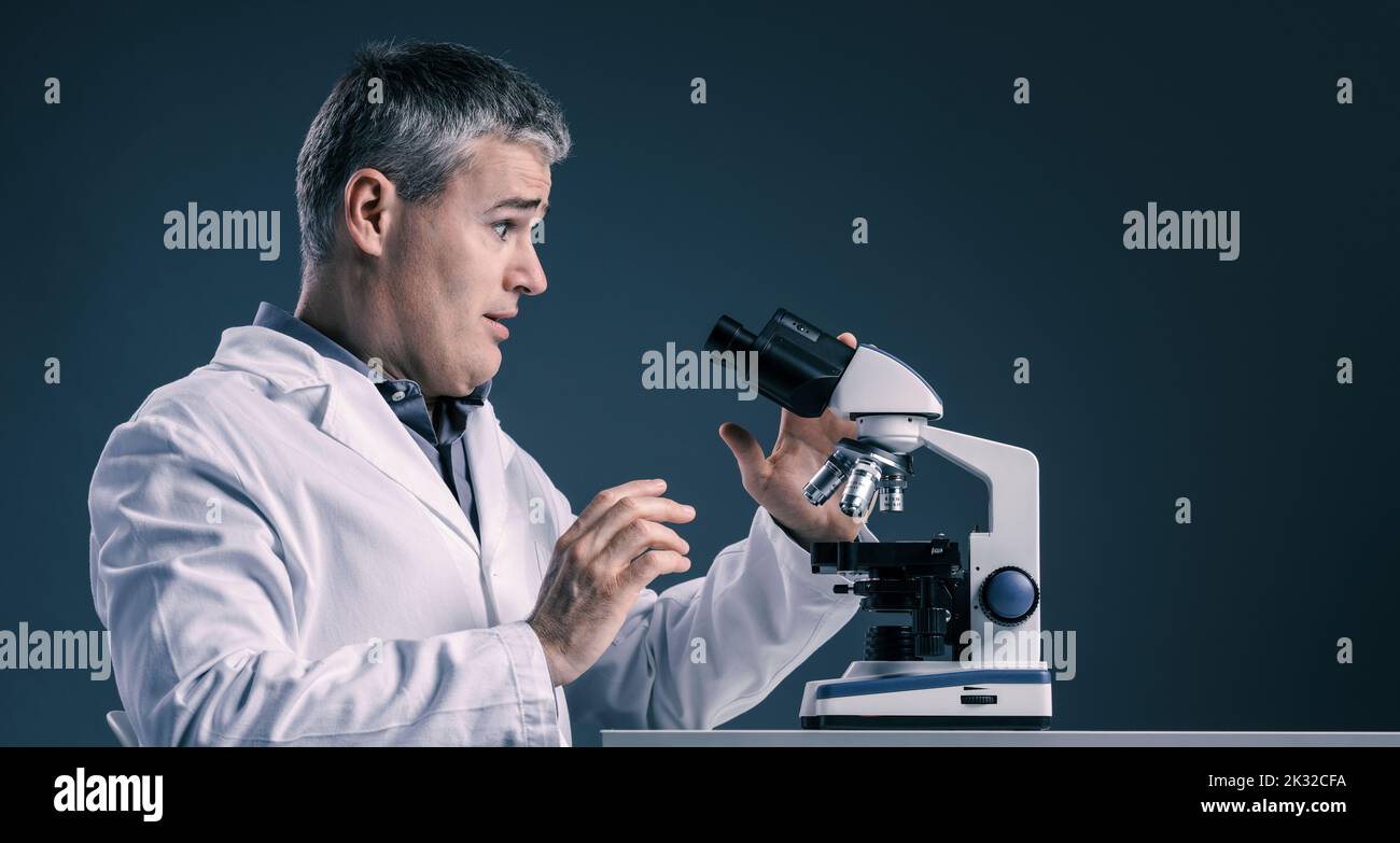 Funny shocked medical scientist working with a microscope, he made an ...
