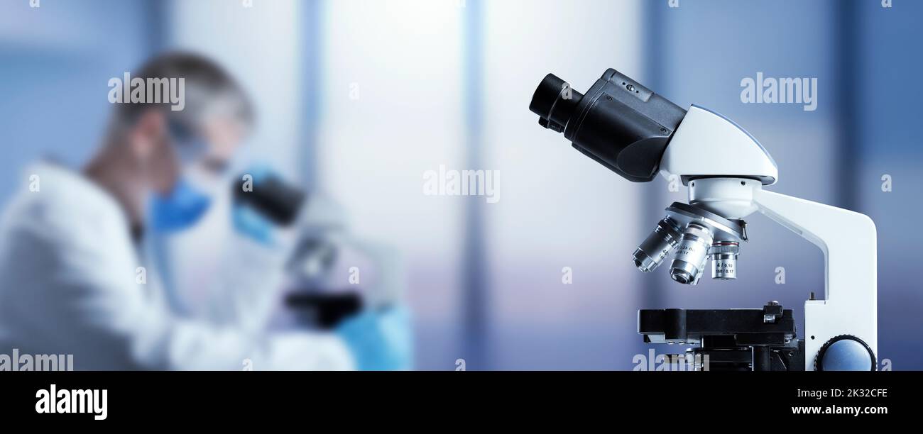 Scientist with face mask examining a sample under the microscope ...