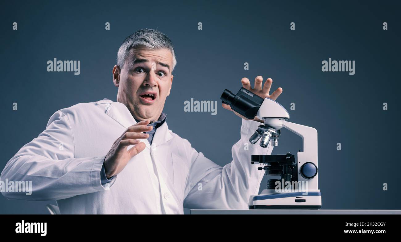 Funny shocked medical scientist working with a microscope, he made an ...