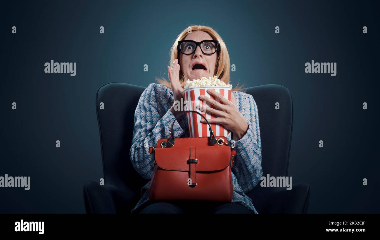 Funny scared woman watching a horror movie and eating popcorn, cinema ...