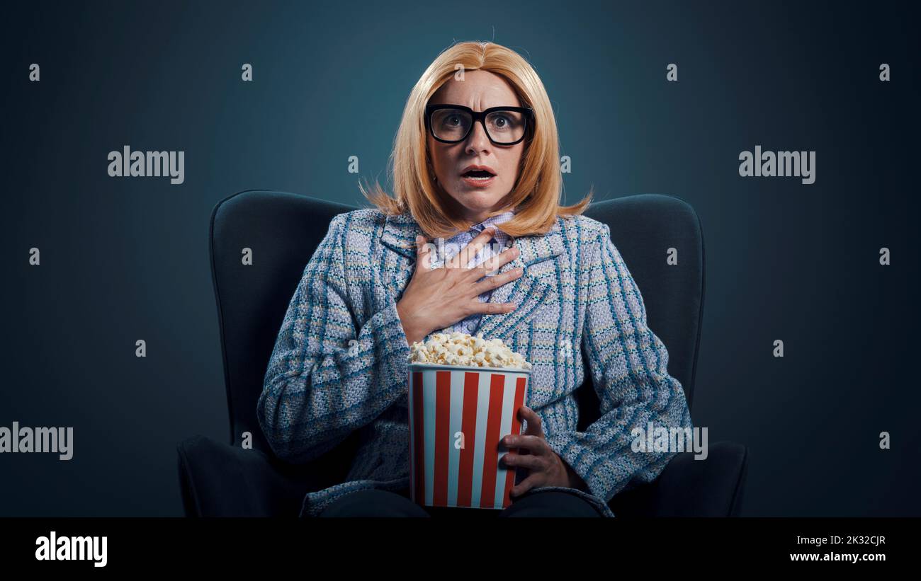 Funny woman watching a suspense movie and eating popcorn at the movie ...