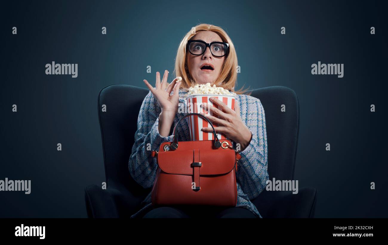 Funny scared woman watching a horror movie and eating popcorn, cinema ...