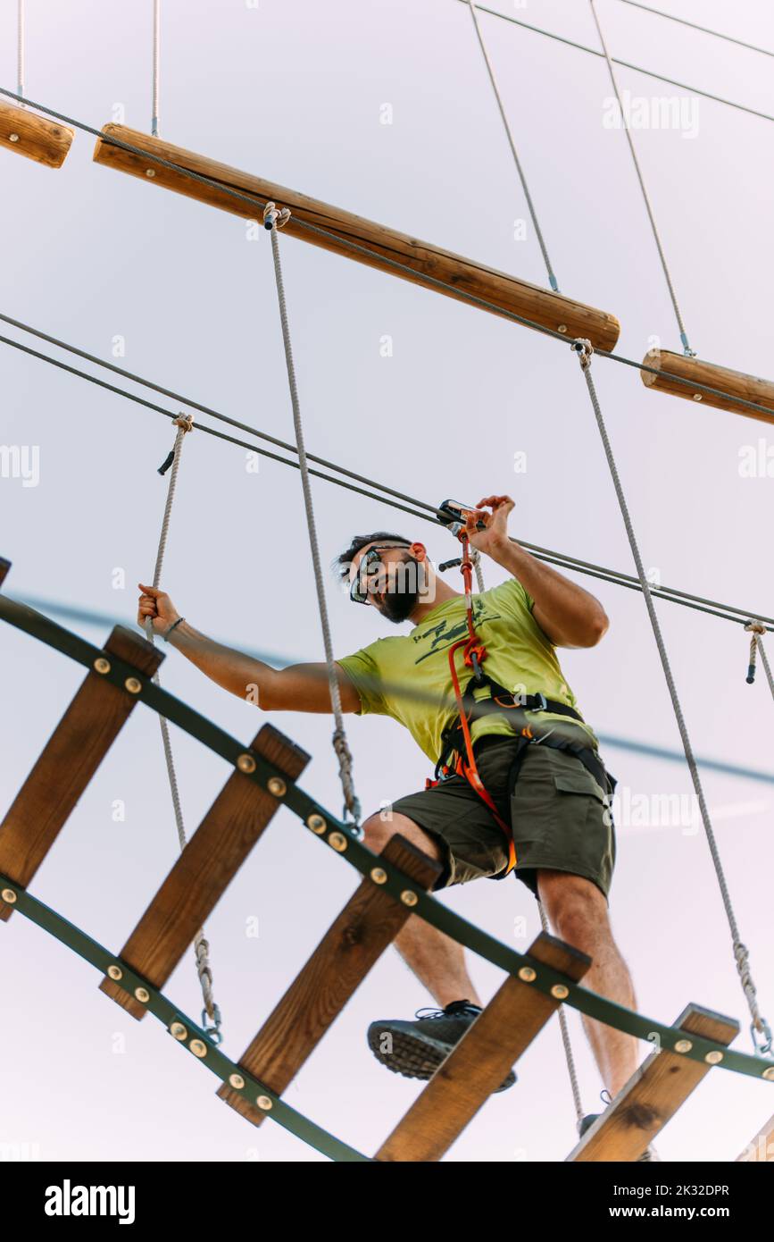 Handsome man balancing himself on the ladder in the adventure park ...