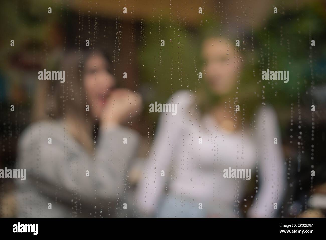 Rain drops in focus, two girls eating in lucnh bar while being in blur ...