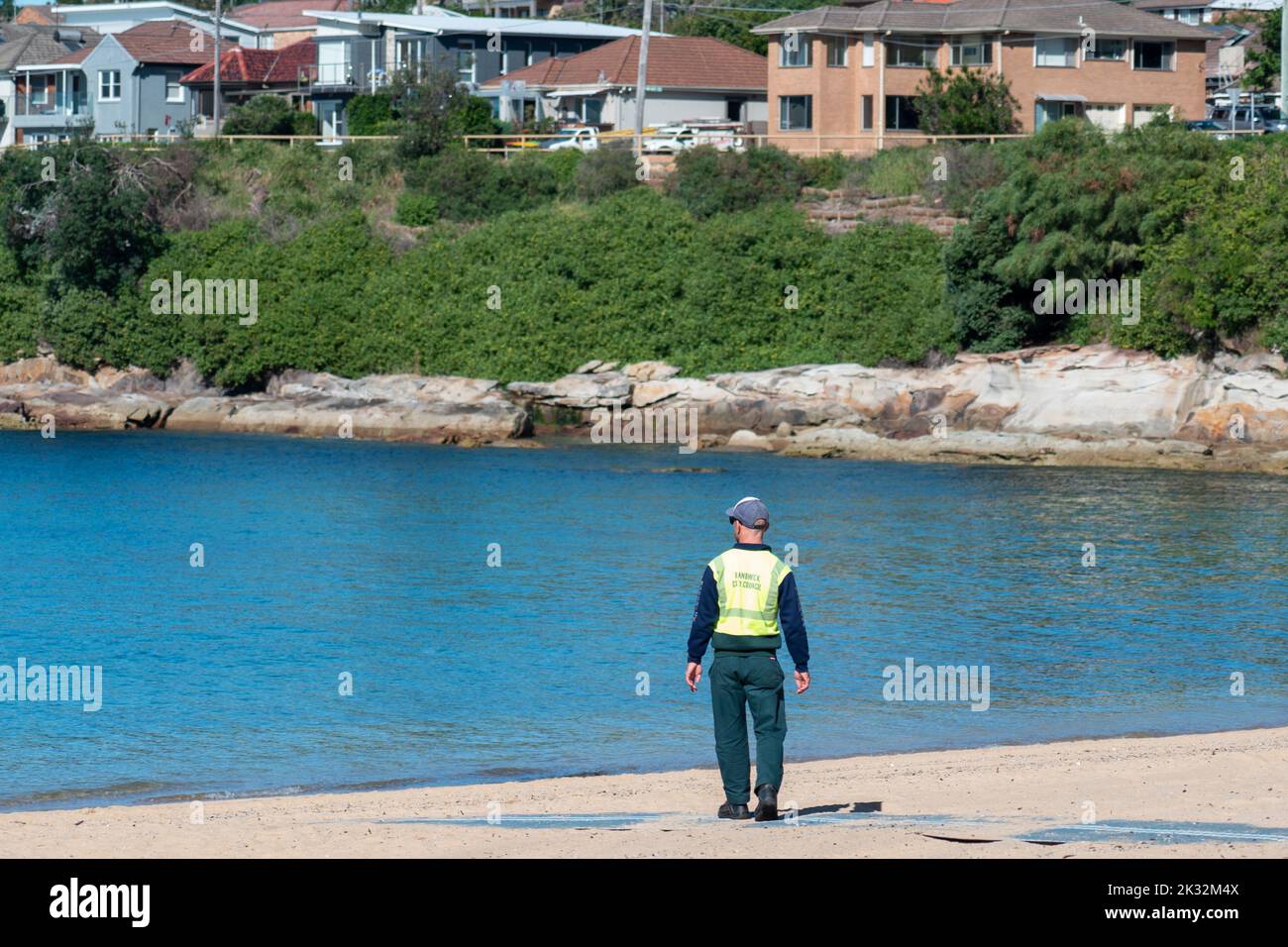 A council worker facing backward cleaning the beach while wearing a ...