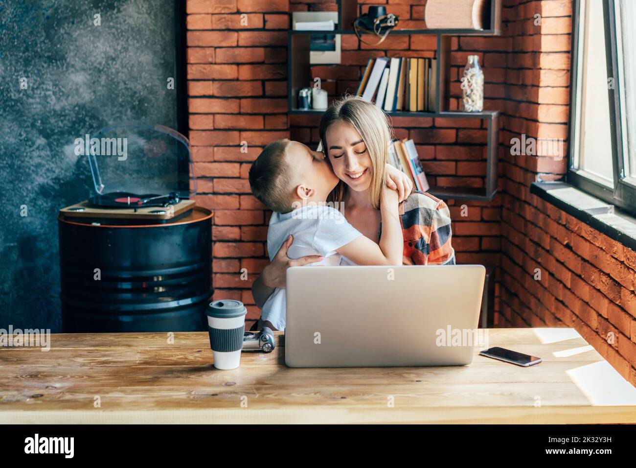 Son hugs mother working on laptop. Family bonding, mom and son use ...