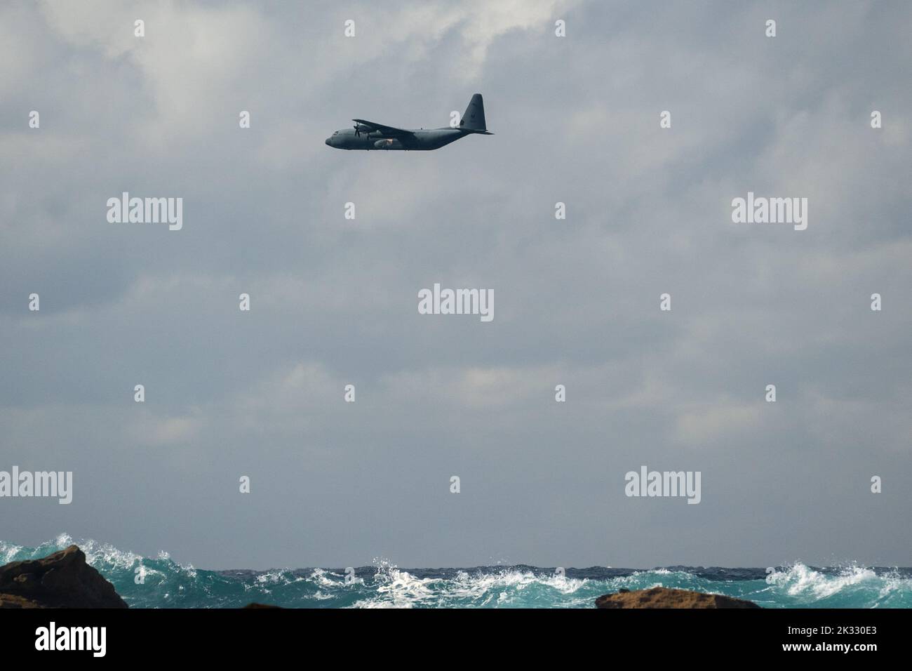 A passenger plane flying over a sea on a cloudy day with rocks and ...