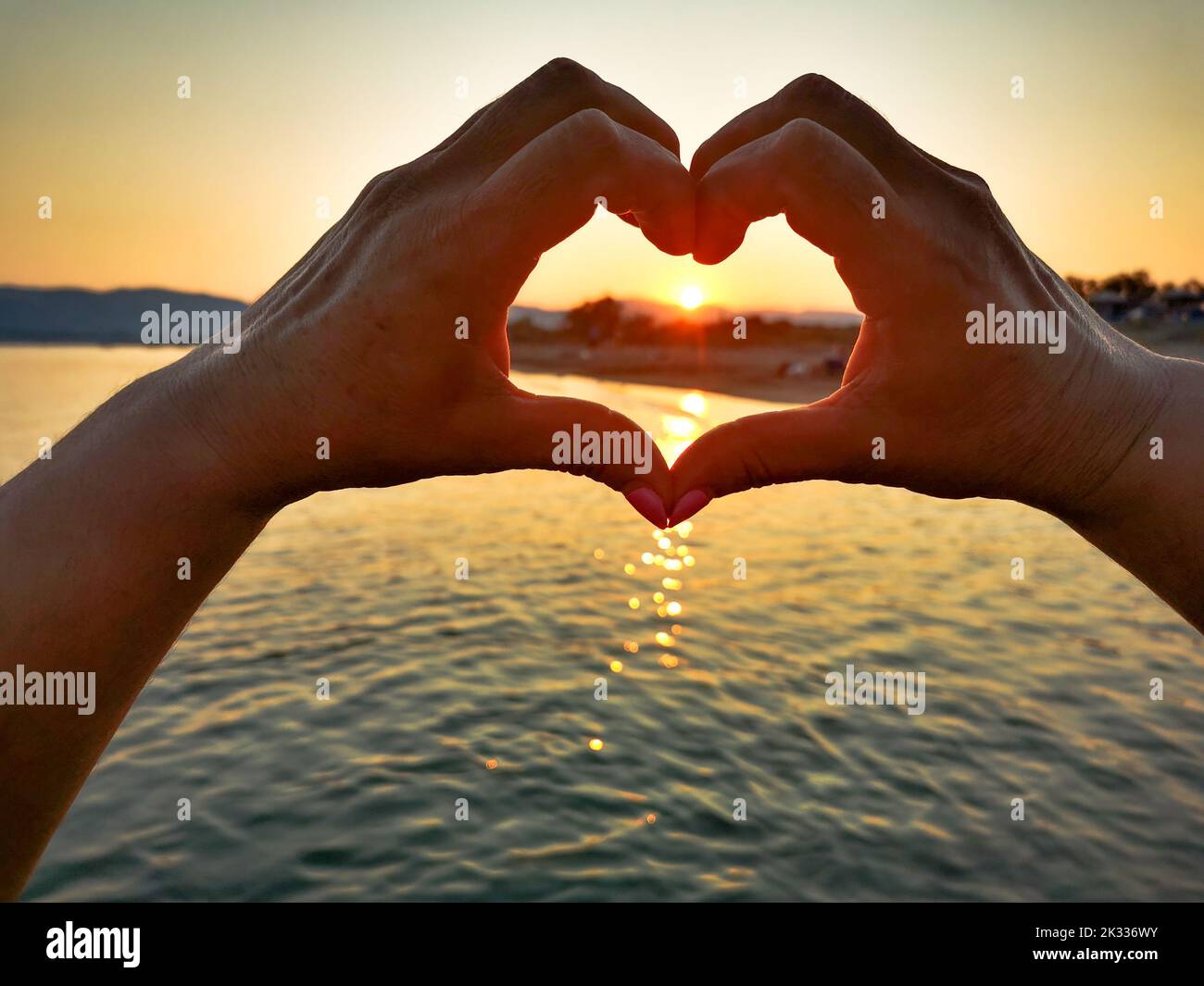 Senior woman hands in heart shape love sign around sun during sunset on ...