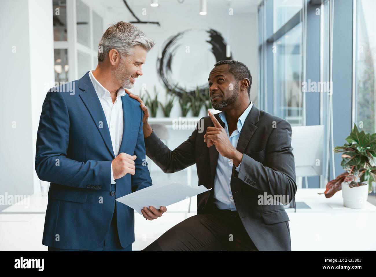 Two businessmen talking about deal standing in meeting room in modern ...