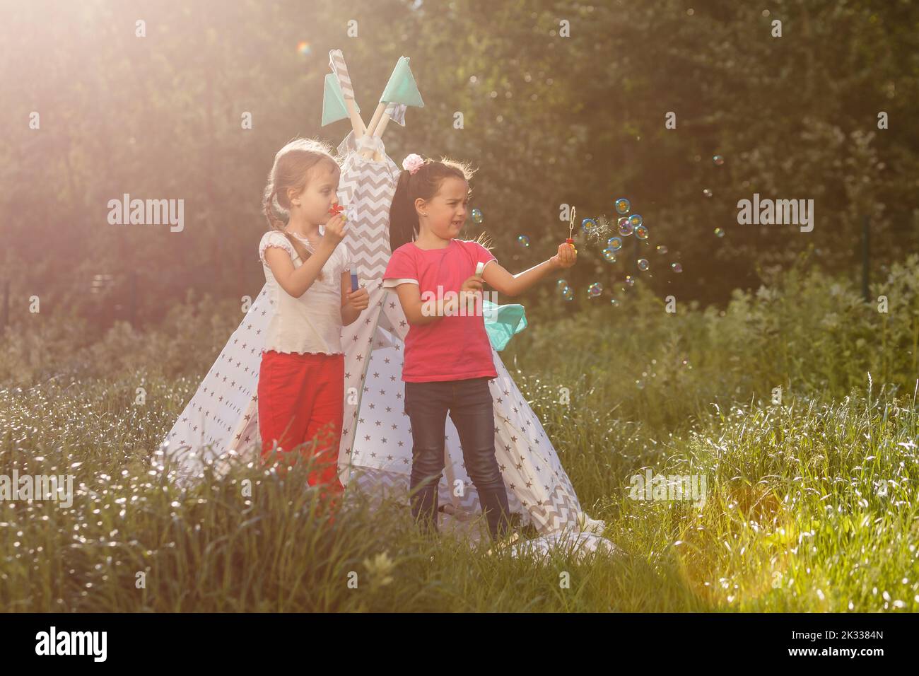 Two happy laughing little girls in camping tent in dandelion field ...