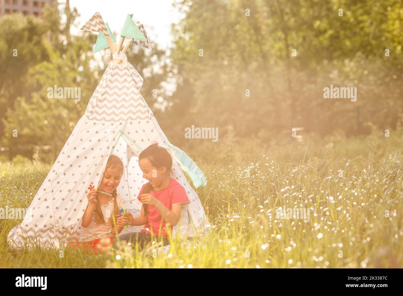 Two happy laughing little girls in camping tent in dandelion field ...