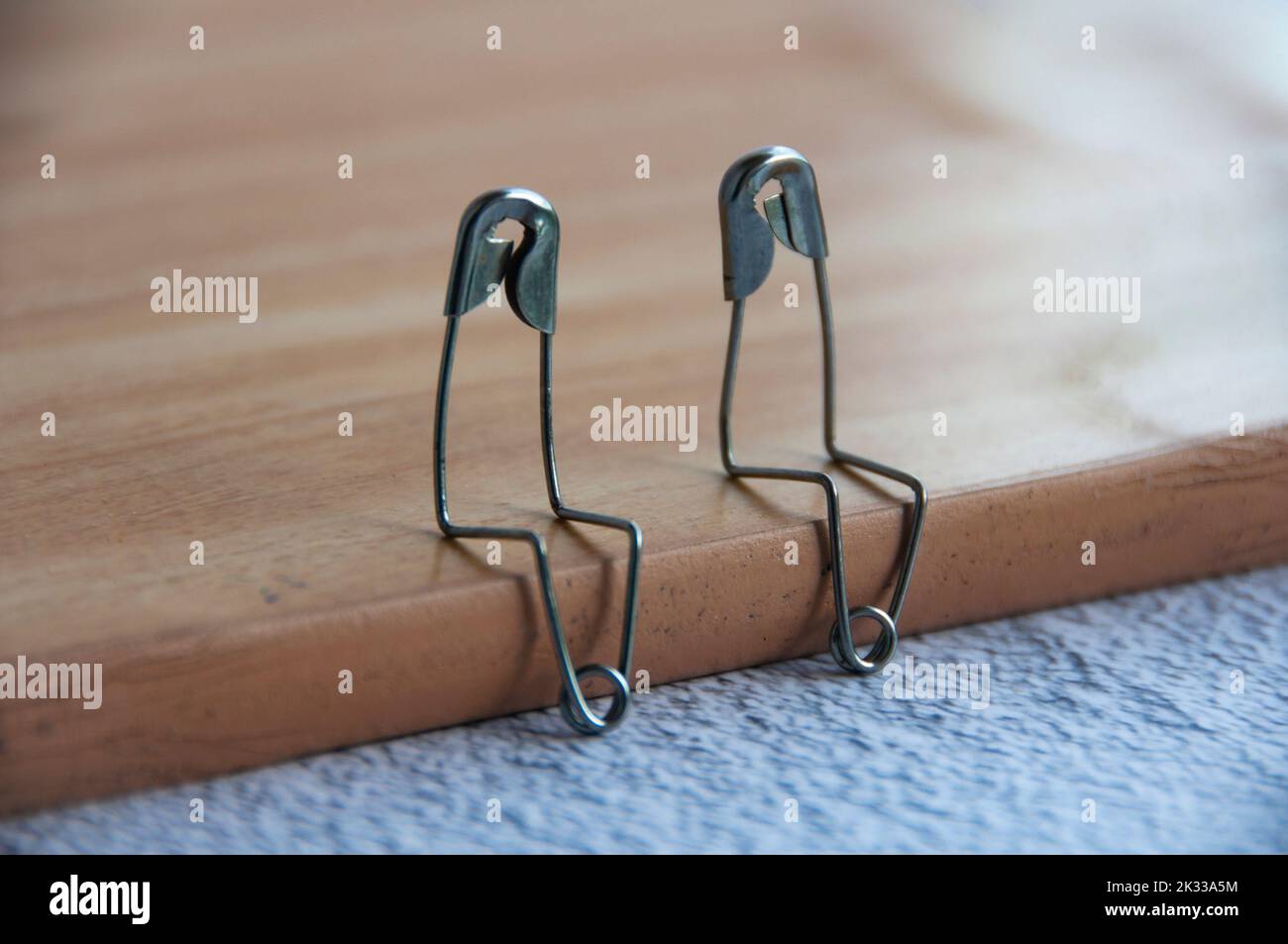Two safety pins sitting on brown wood having a conversation. Friendship ...