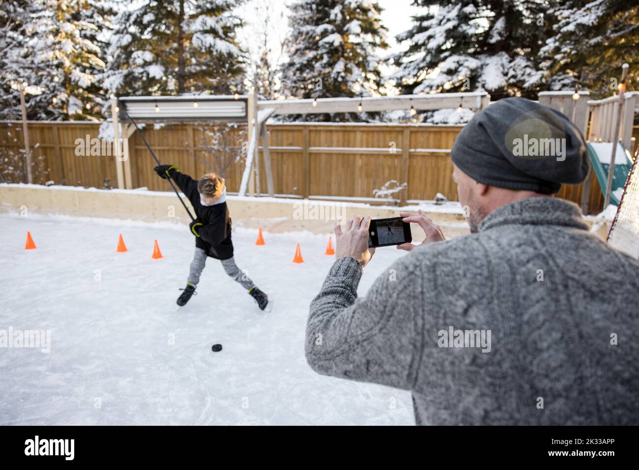 Father photographing son practicing ice hockey shot on goal on rink ... Father photographing son practicing ice hockey shot on goal on rink ...