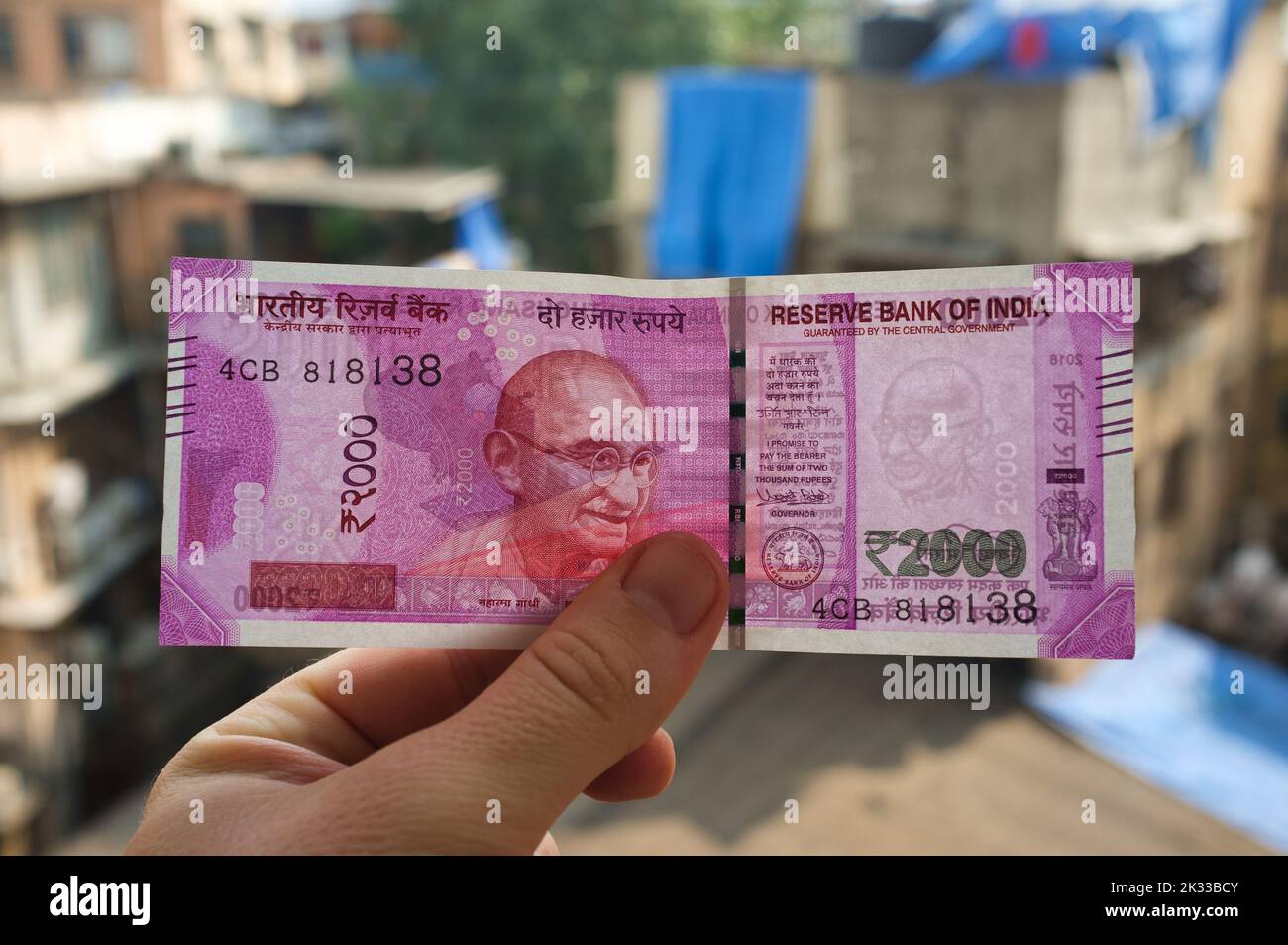 A male hand holding Indian two thousand rupee pink banknote with ...