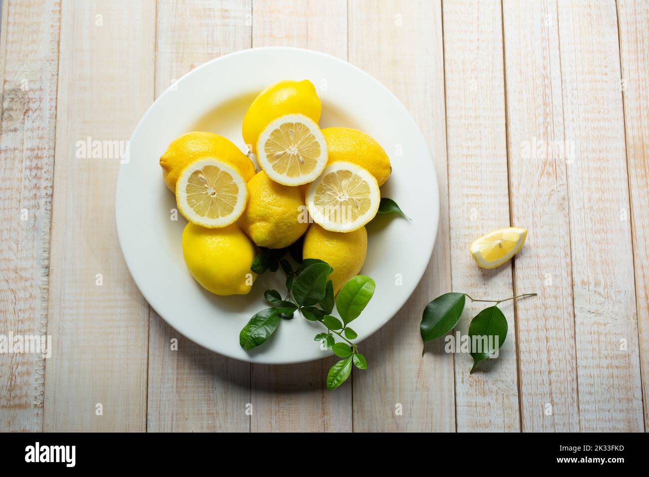 A top view of a nicely decorated white plate of whole and sliced lemons ...