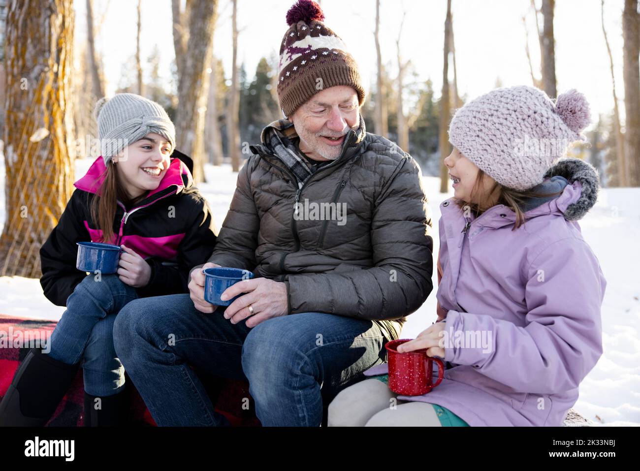 Happy grandpa and granddaughters enjoying hot cocoa in winter woods ...