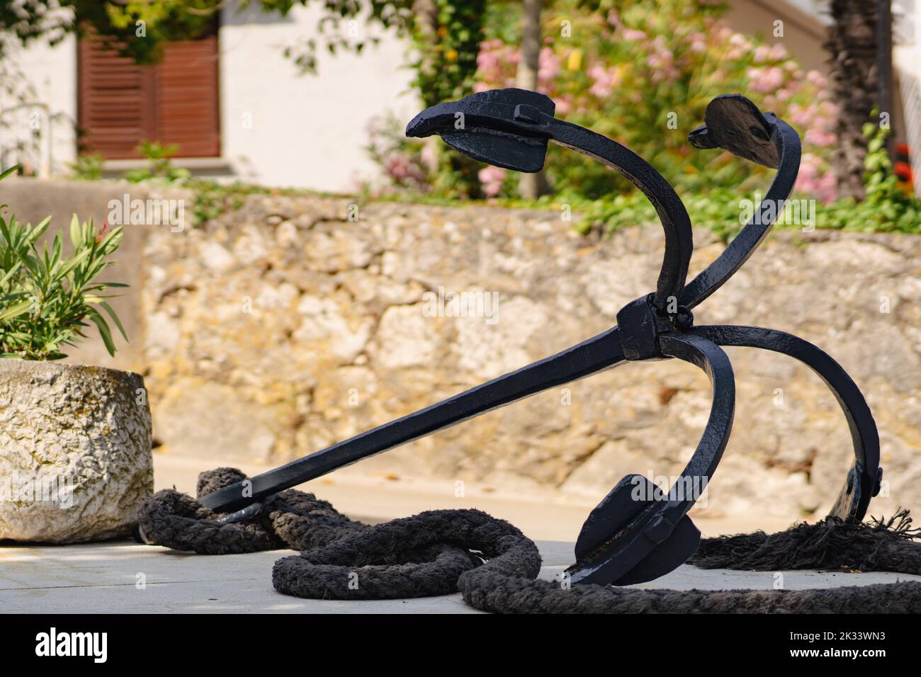 A closeup of a black anchor with a thick rope tied to it laying on the ...