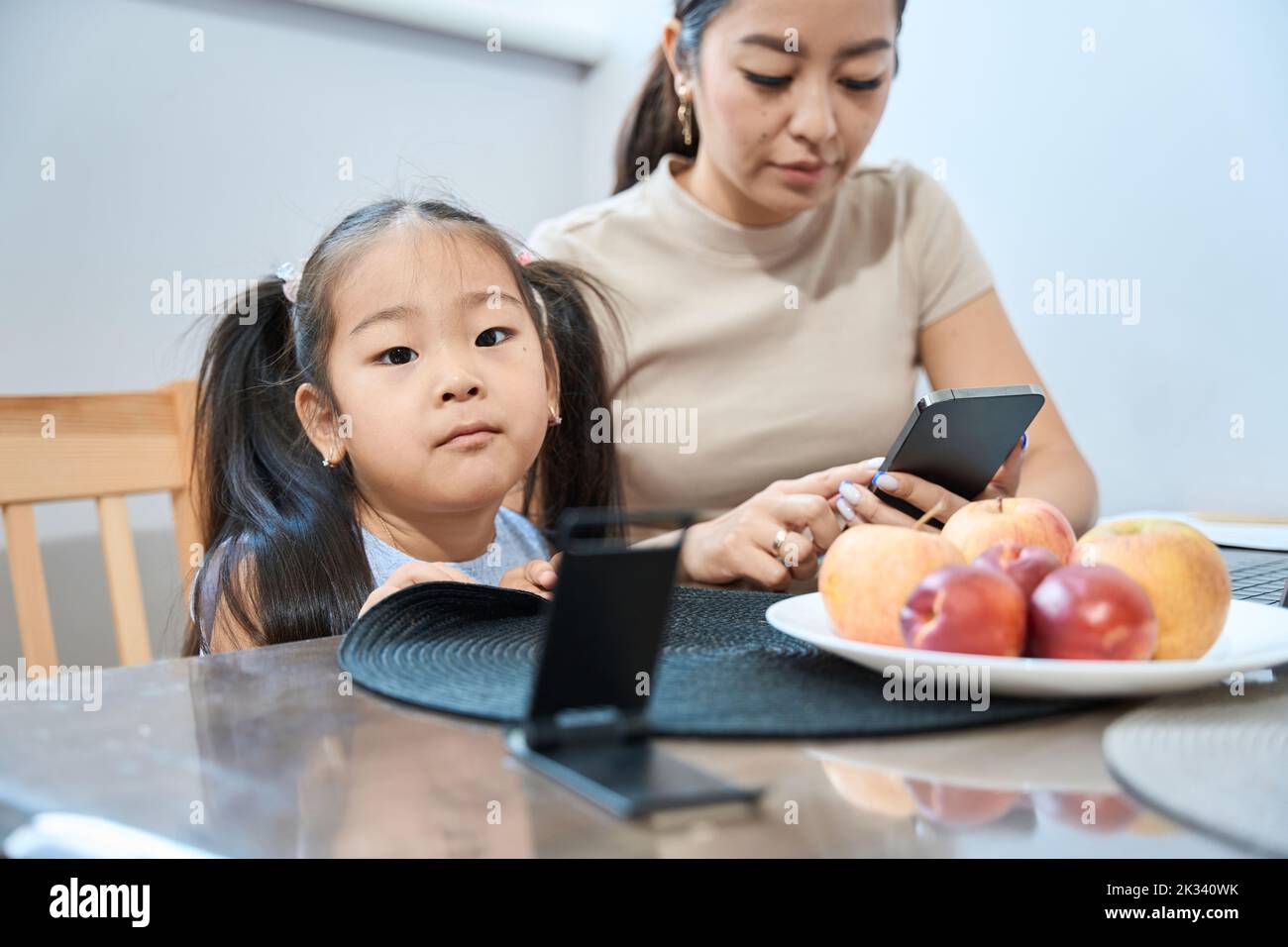 Working mom and bored daughter sitting at table with gadgets Stock ...