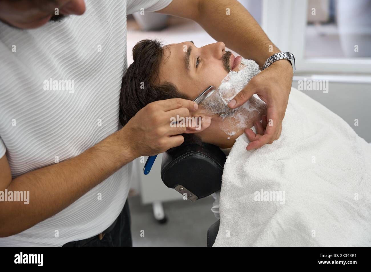 Skilled barber performing a clean shave for a client face Stock Photo ...