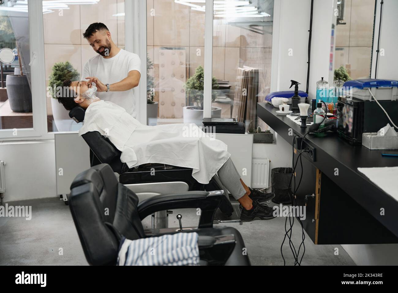 Pleasant barbershop worker performing a clean shave for brunet ...