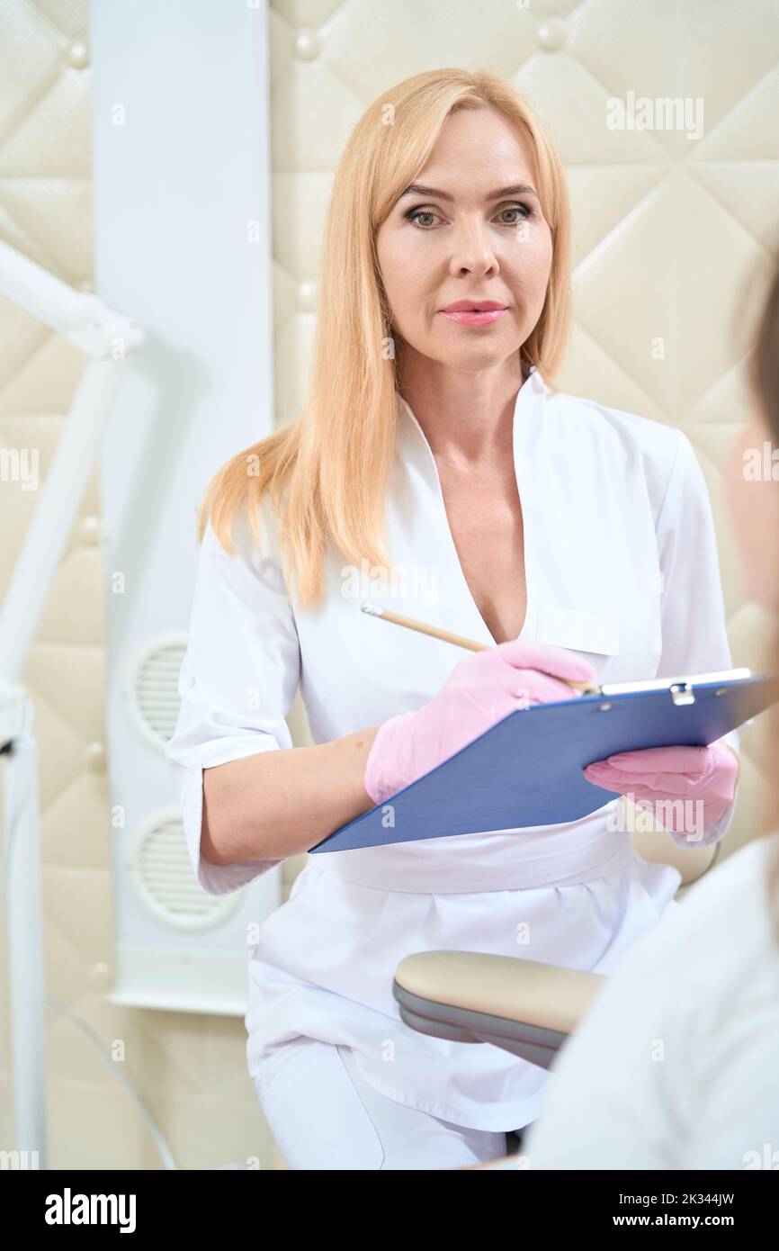 Attractive female dermatologist sits in chair and holds blue folder ...