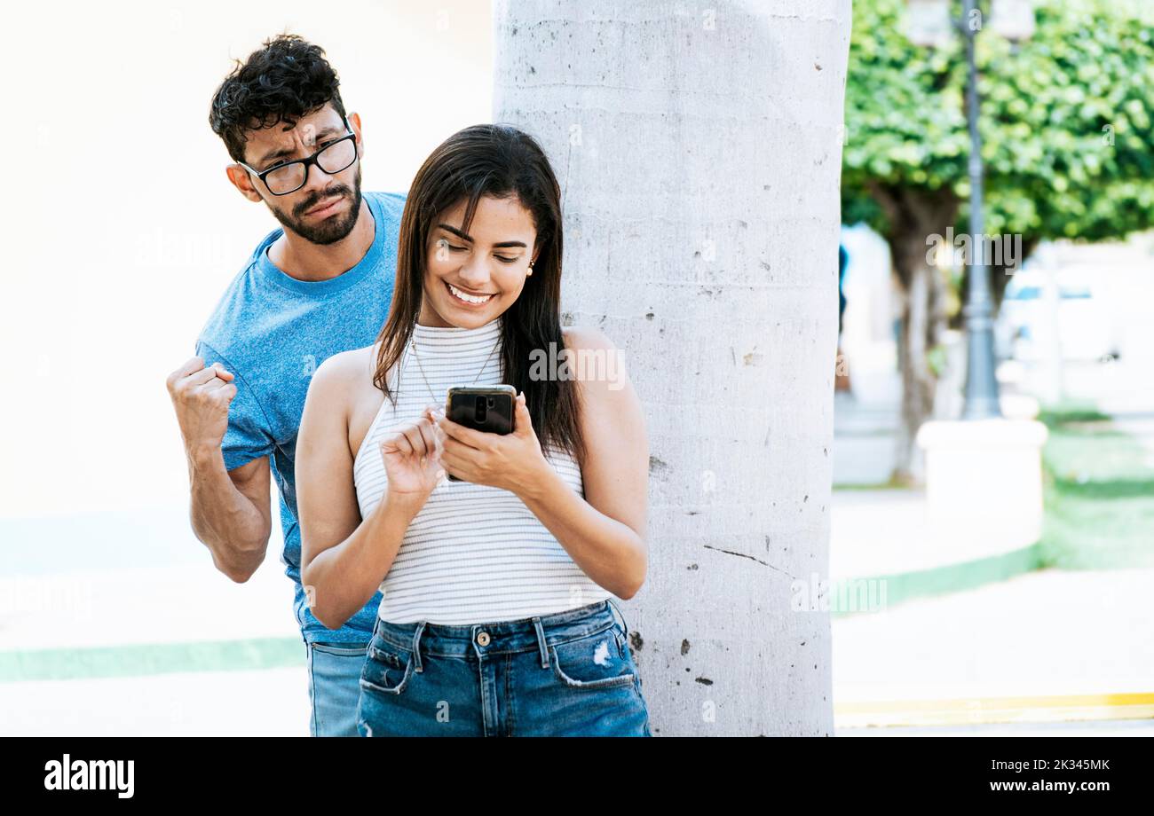 Jealous man spying on his girlfriend texting on the cell phone. Suspicious man spying on his ...