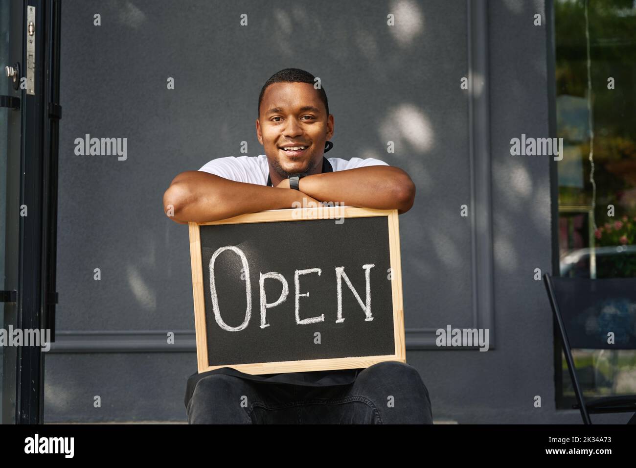 Smiling young man holding an open sign Stock Photo - Alamy