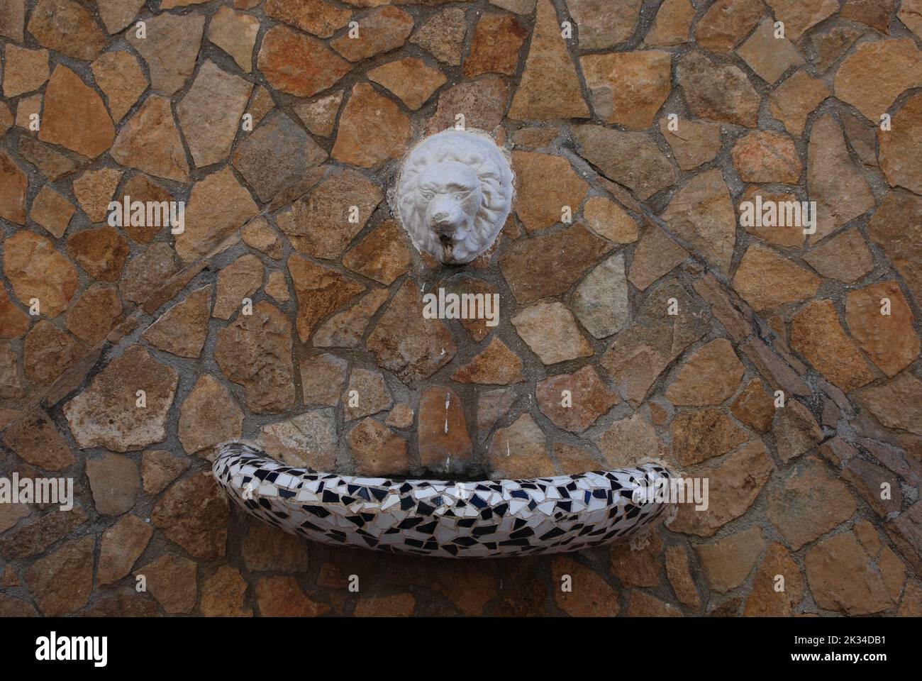 A closeup shot of a mosaic wall with a lion head sculpture and water ...
