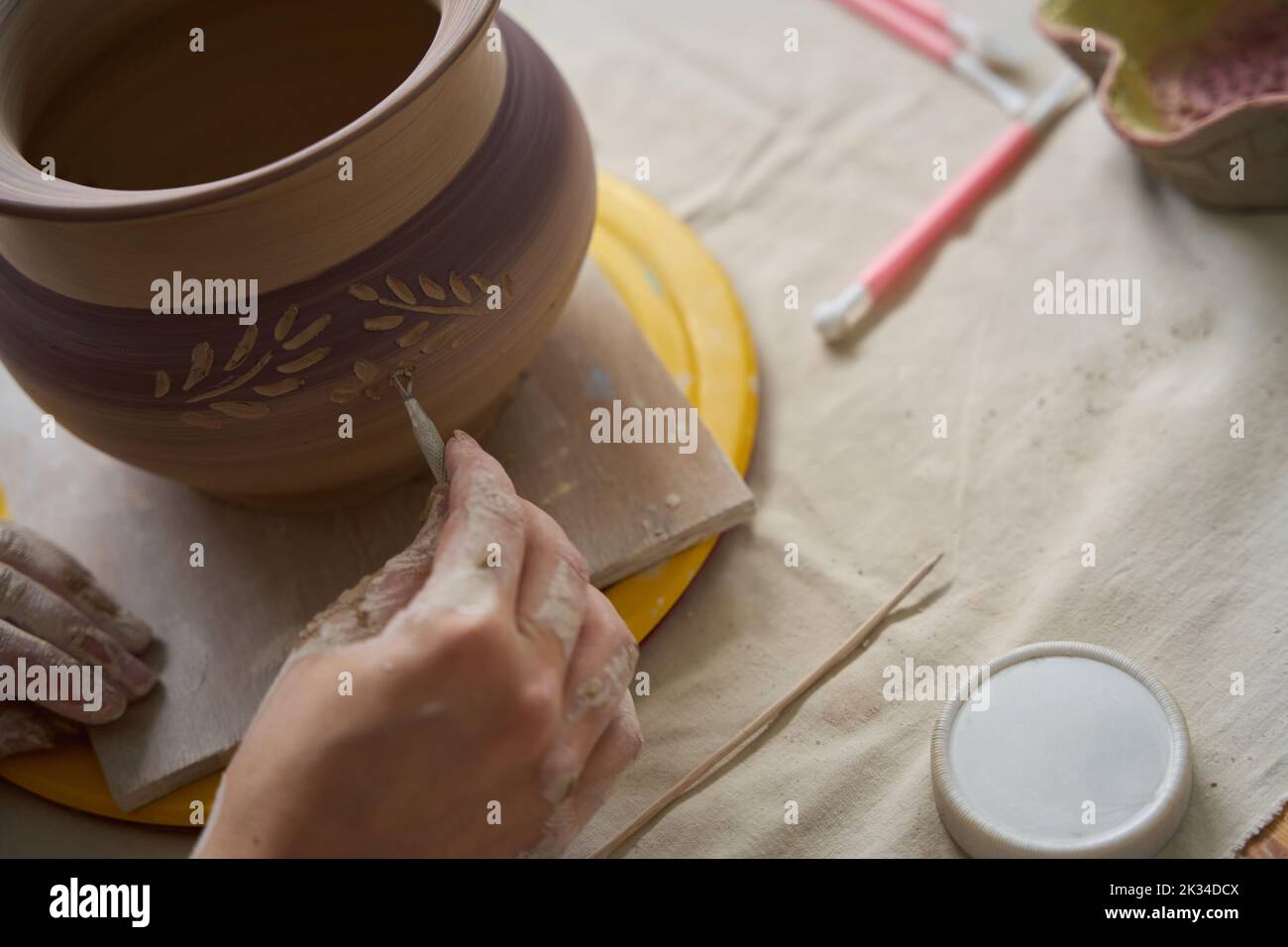 Craftswoman sits at table and works with loop on vase Stock Photo - Alamy