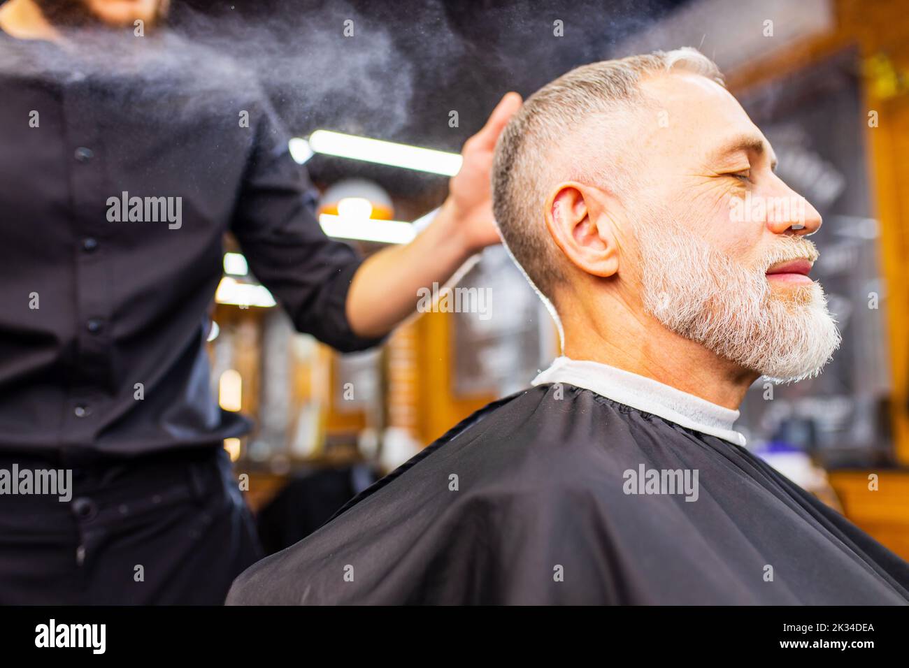 retired man visiting barbershop , sitting in the barber's chair while ...