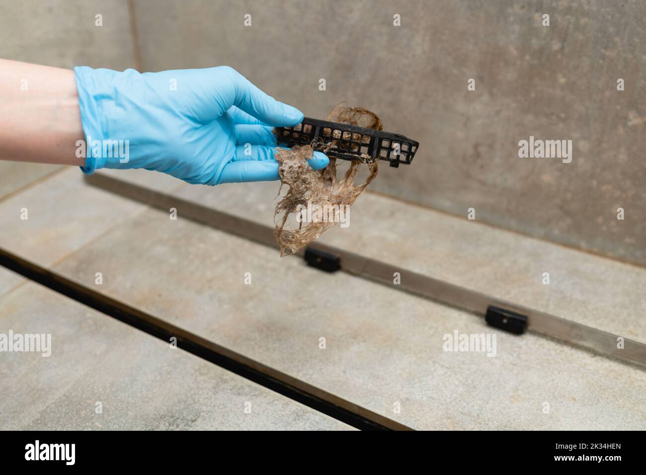 Woman removing hair clump from the shower drain. Female hand in a blue ...