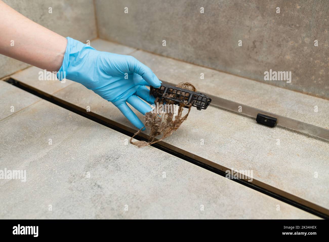 Woman removing hair clump from the shower drain. Female hand in a blue ...