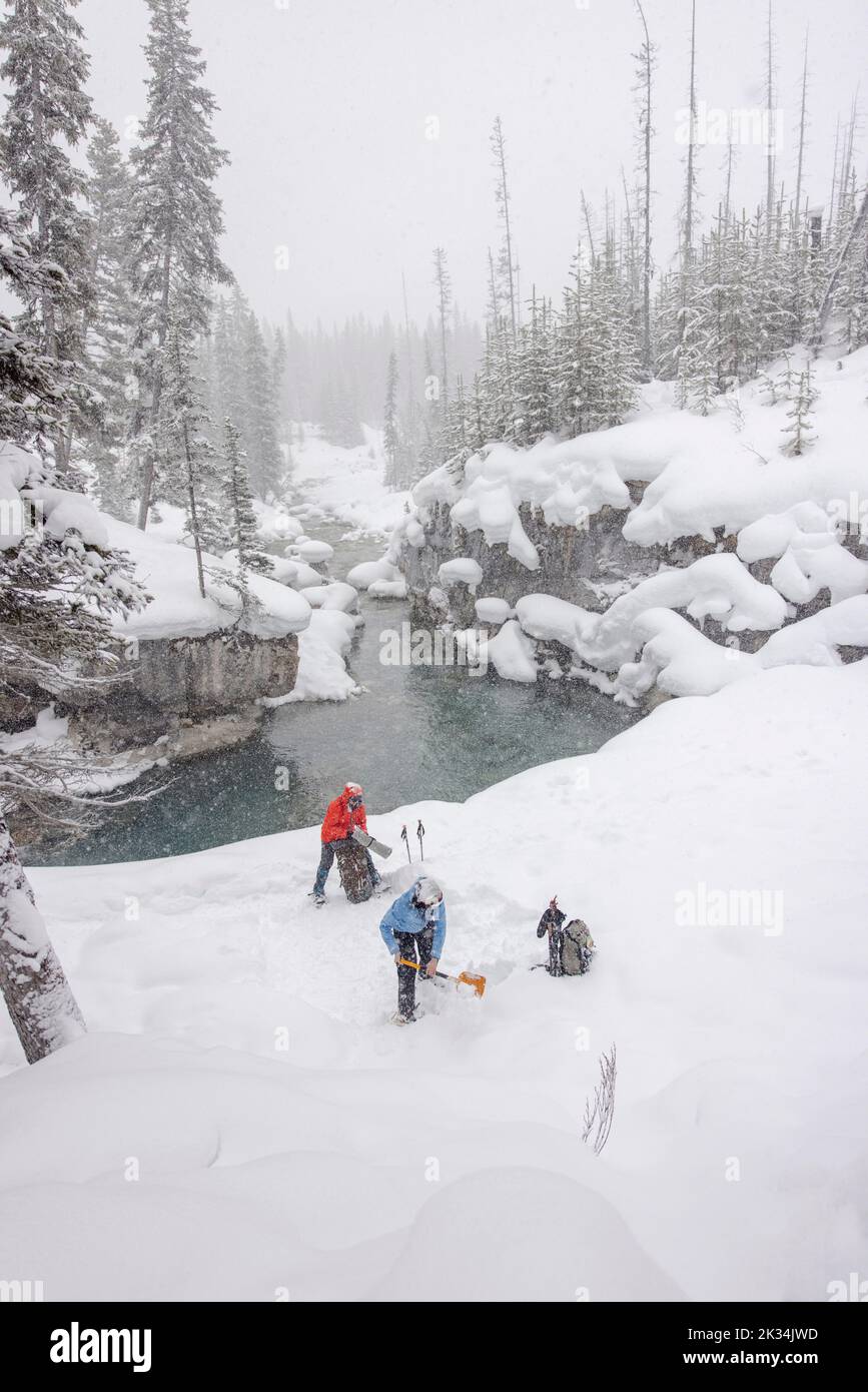 Female snowshoers digging in snow along tranquil winter river Stock ...