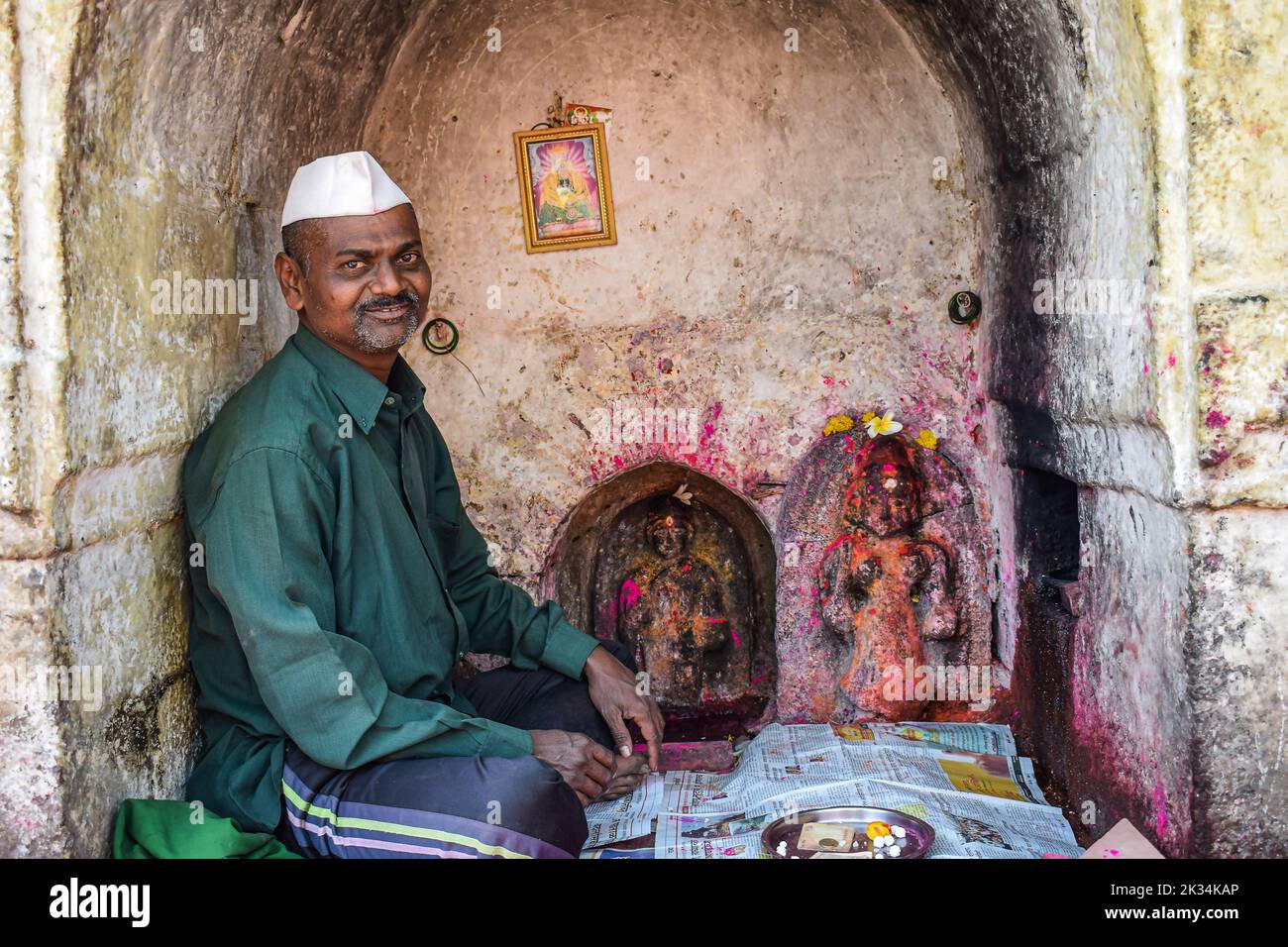 An Indian priest wearing a green shirt, grey pants and white cap ...