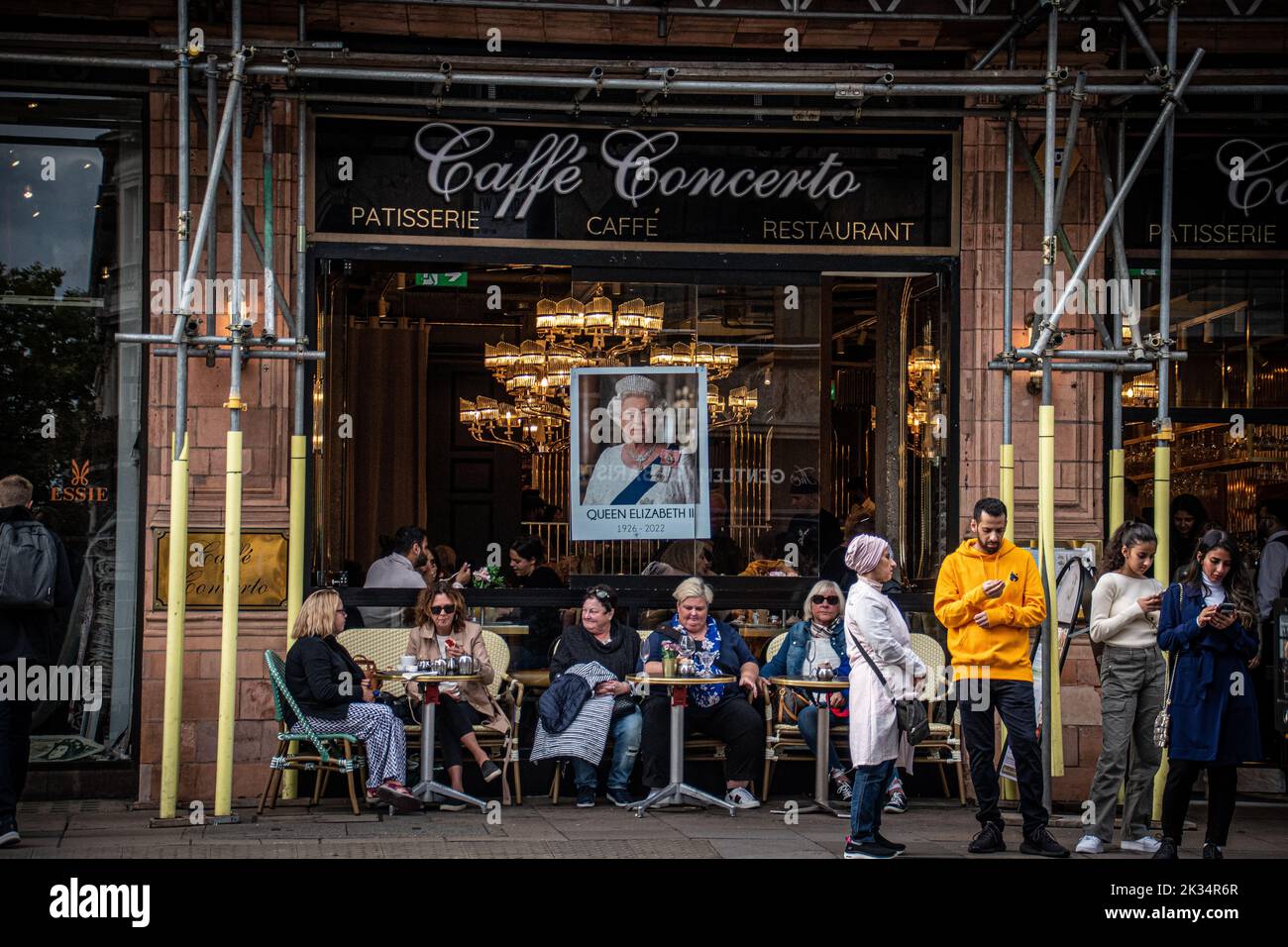 People sat outside a cafe with a poster of The Queen in the window ...
