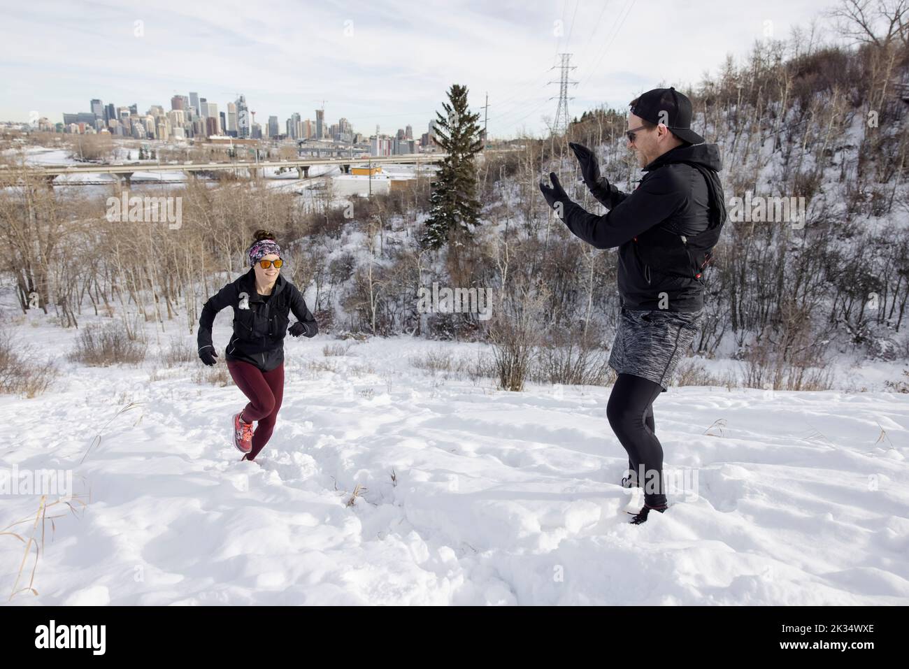 Man clapping hands, encouraging woman running up snow covered slope ...