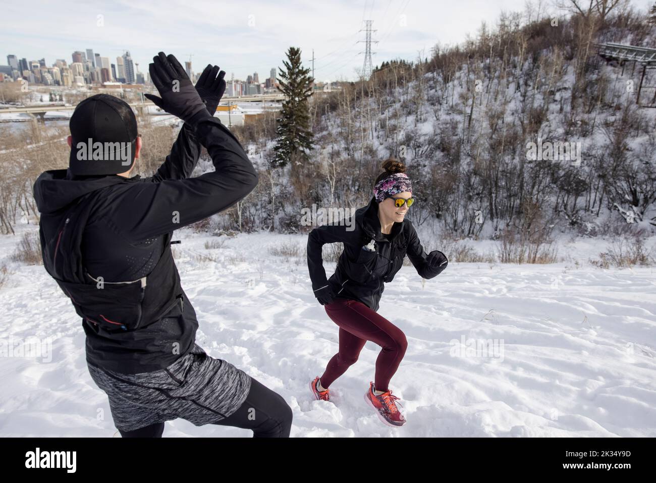 Man clapping hands, encouraging woman running up snow covered slope ...