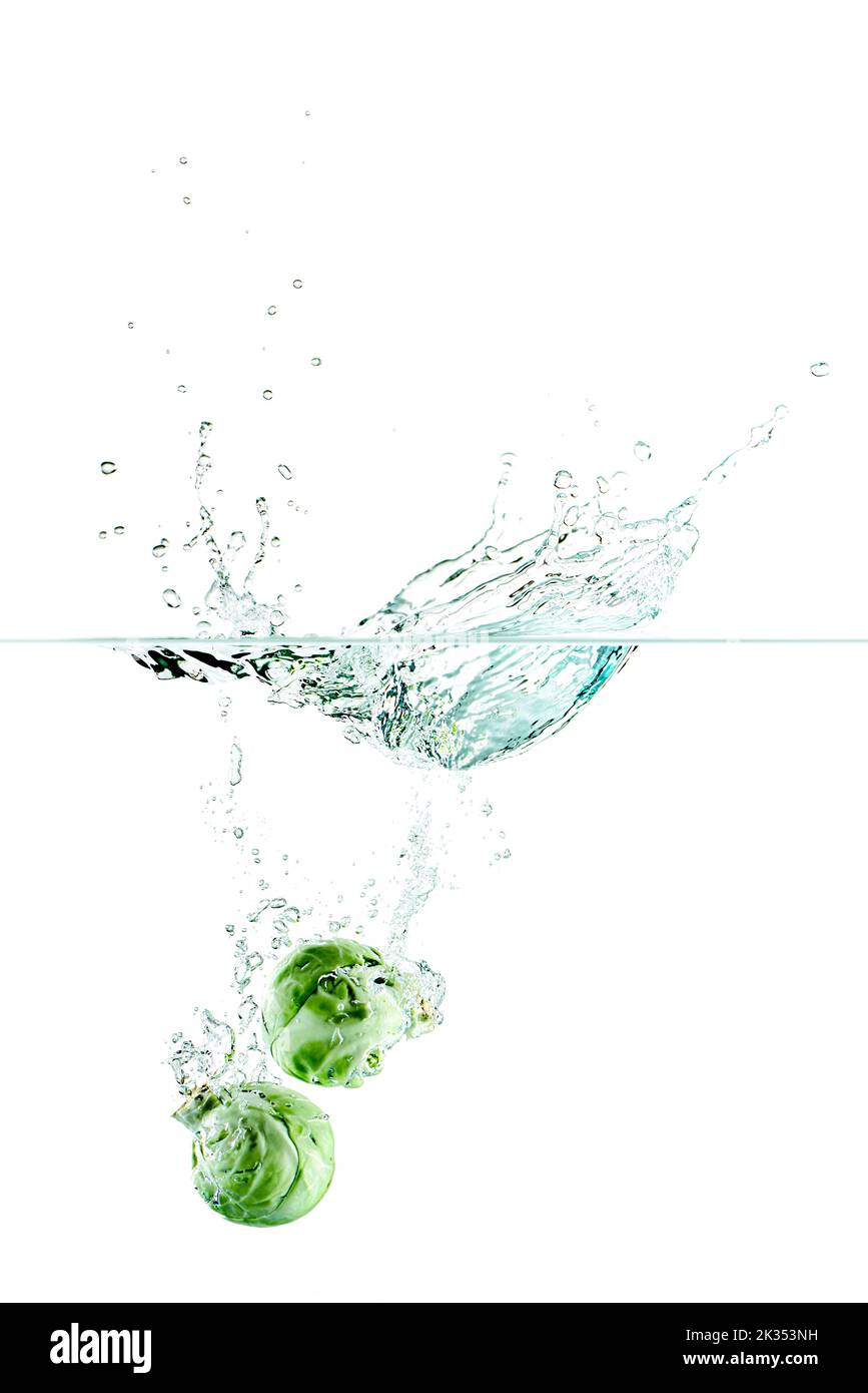 two brussels sprouts falling into water splash on a white background ...