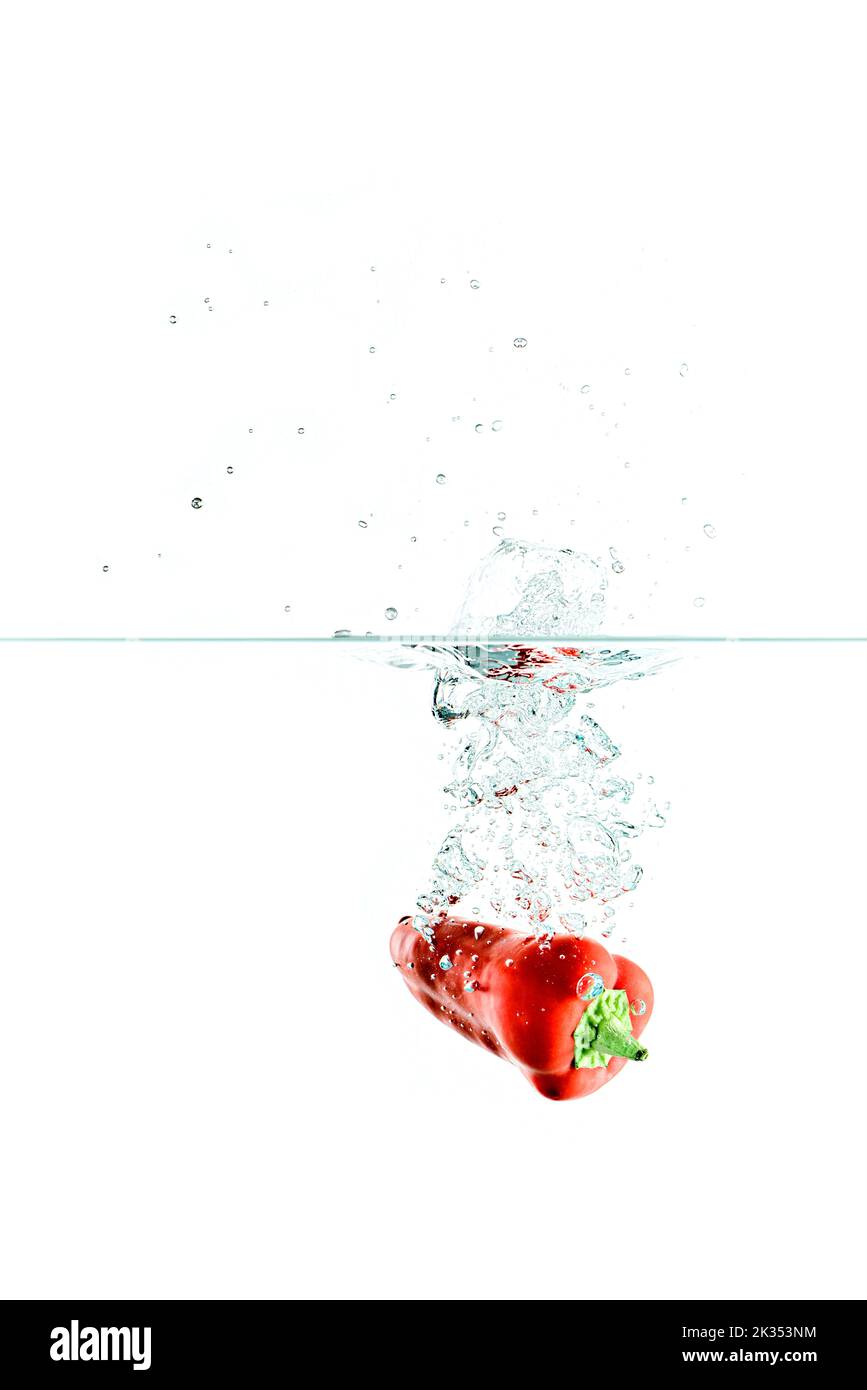 A Red chili pepper falling into water splash on a white background ...