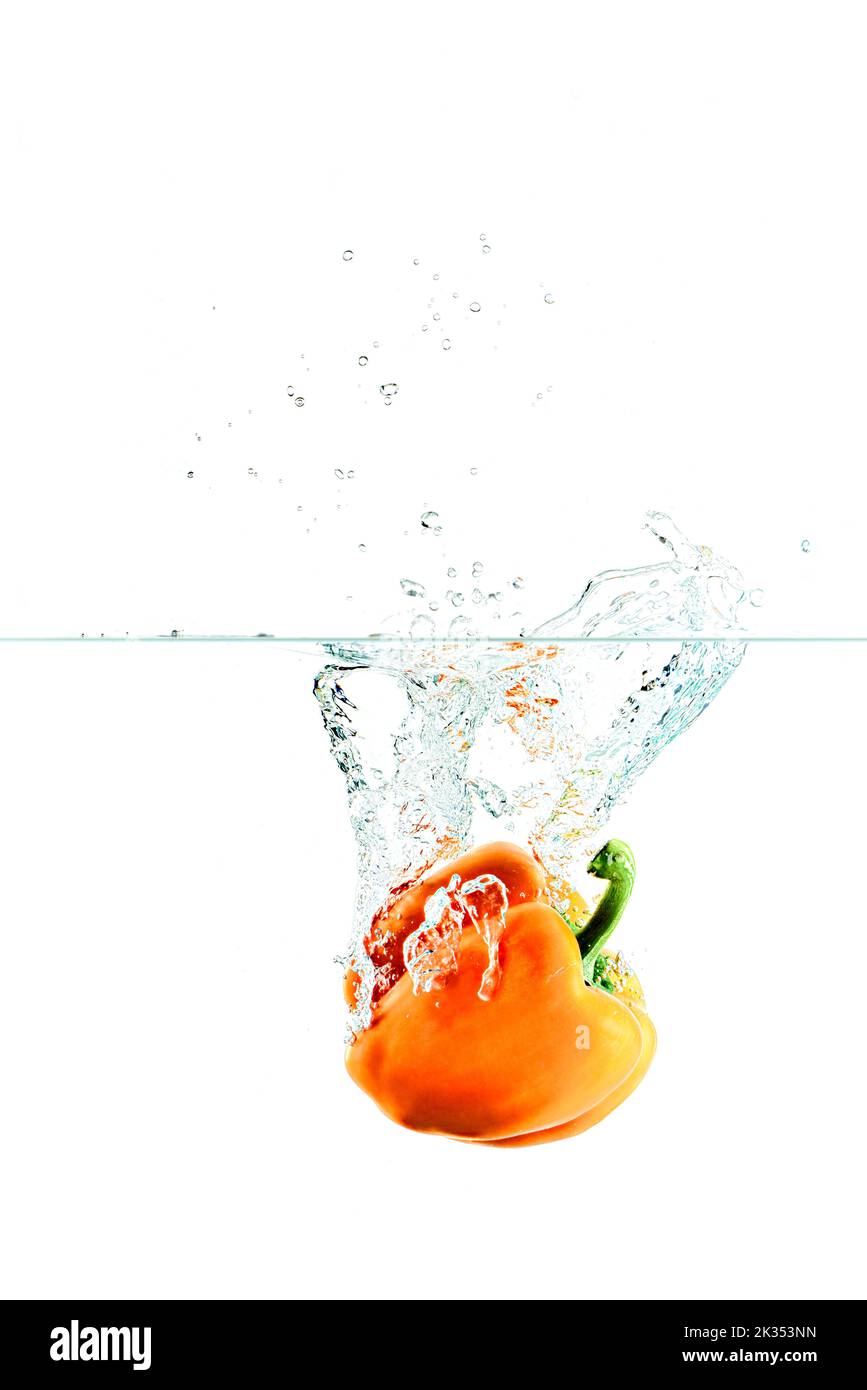 An Orange bell pepper falling into water splash on a white background ...