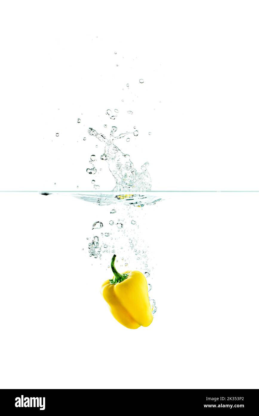 A yellow bell pepper falling into water splash on a white background ...