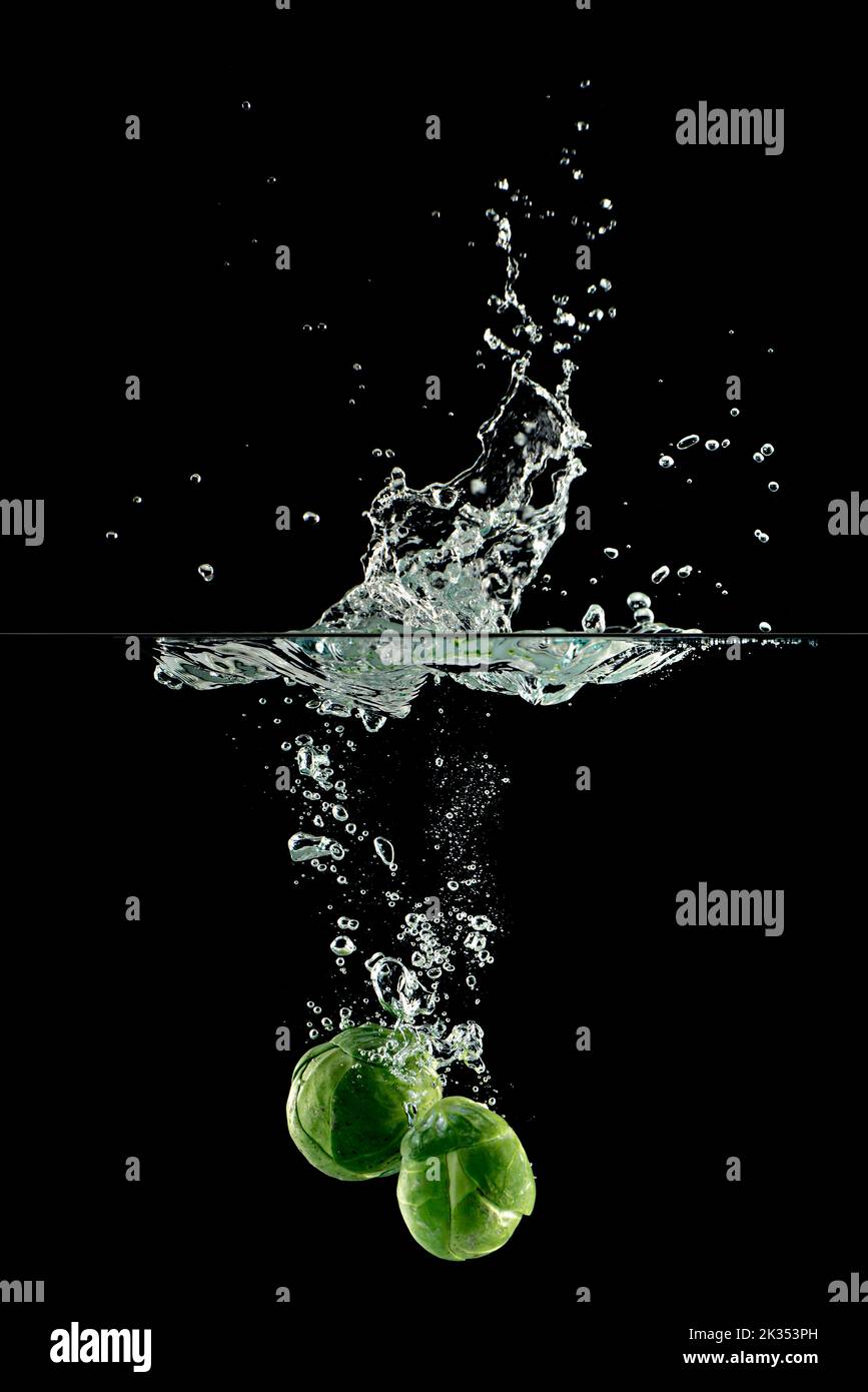 Two Brussels sprouts falling into water splash on a black background ...