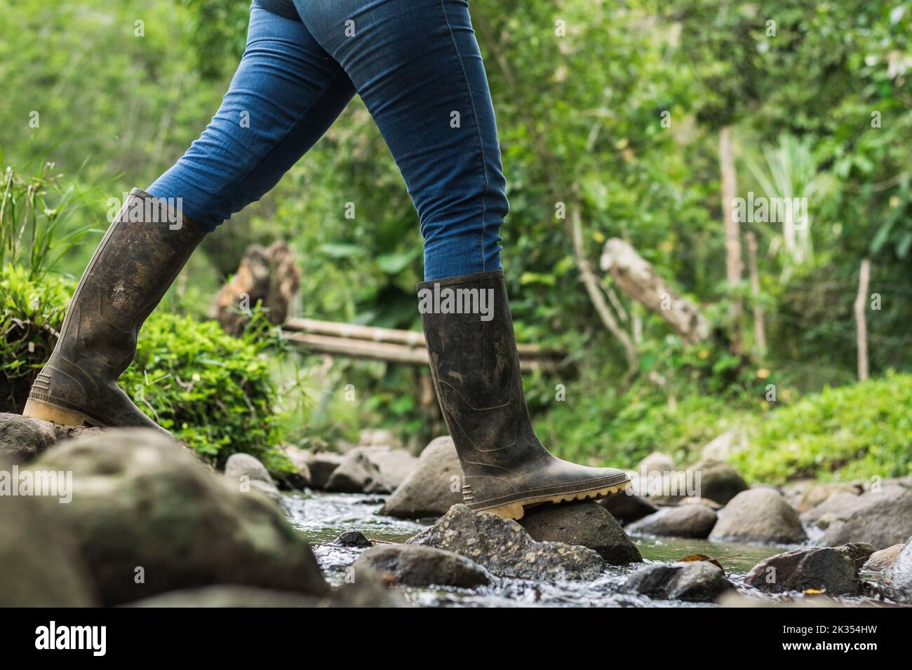 medium shot of a peasant girl crossing a stream in black marsh boots ...
