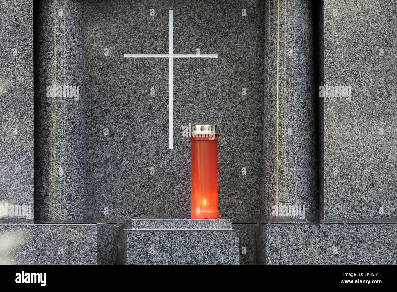 grey marble gravestone with white cross and burning red memorial candle ...