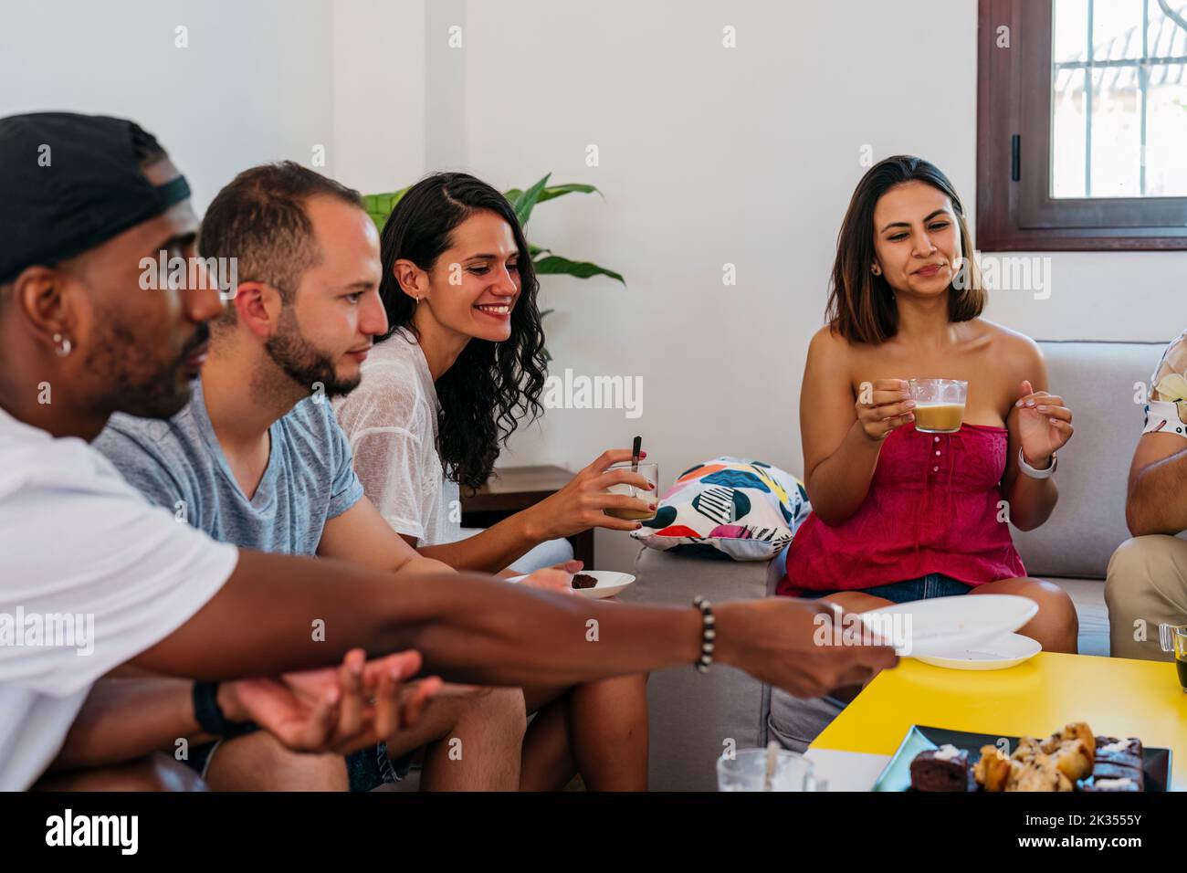 Young latin woman smiles as she drinks coffee while watching a friend ...