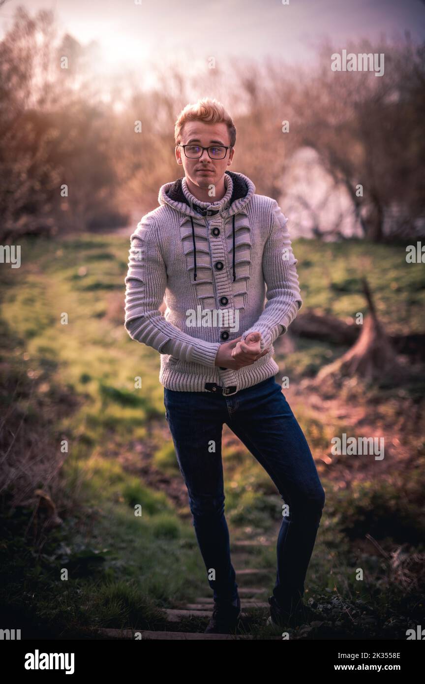 A tall Caucasian man posing standing in a forest with sunlight behind ...