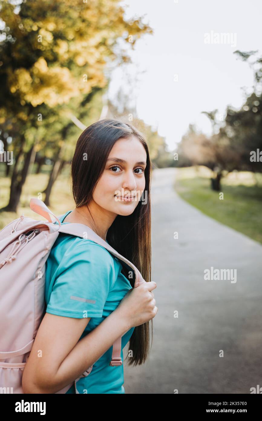 Rear view of student girl, carrying a backpack and looking at the ...