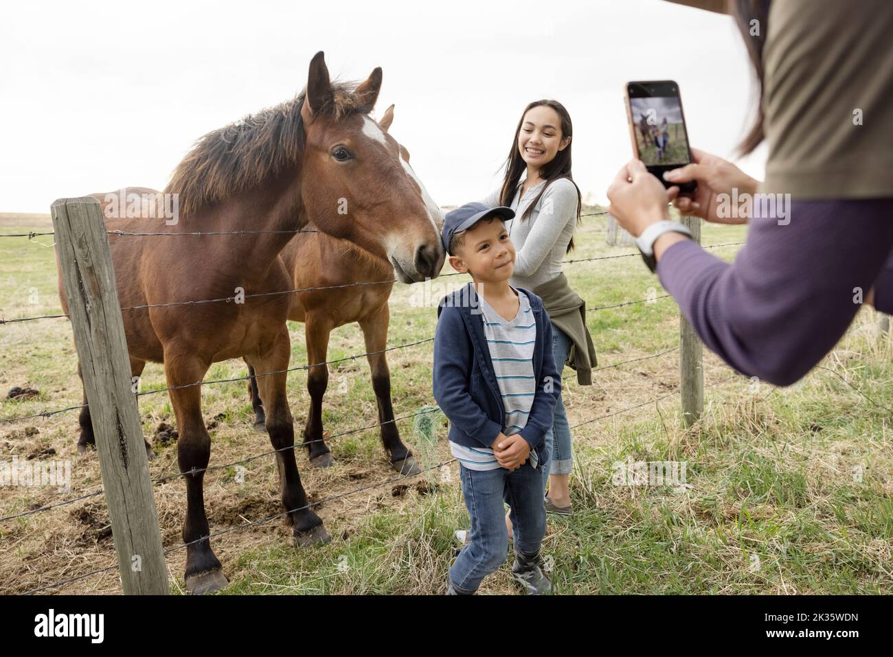 Brother and sister posing for photo with horses at fence on rural farm ...