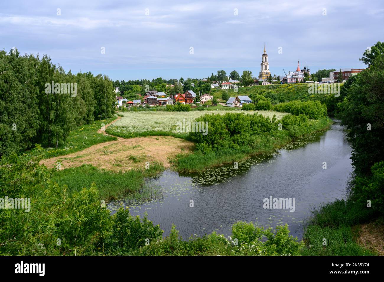 View of the pond, blooming meadow, forest, bell tower, churches and ...
