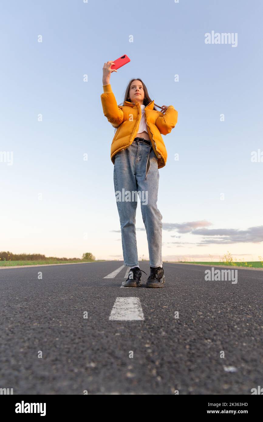 Cool modern teen girl poses on a lonely road while the sky background ...